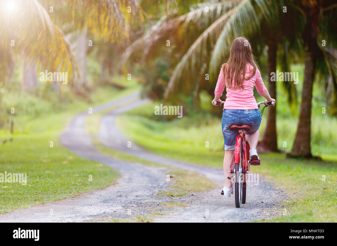 Back view of young woman biking at tropical settings having fun Stock ...
