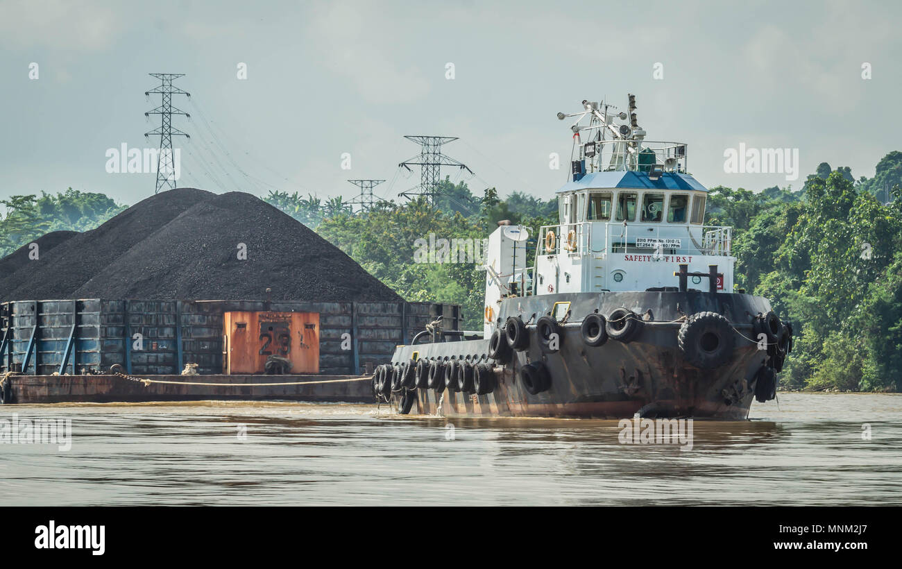 tugboat pulling heavy loaded barge of black coal in the Mahakam river ...