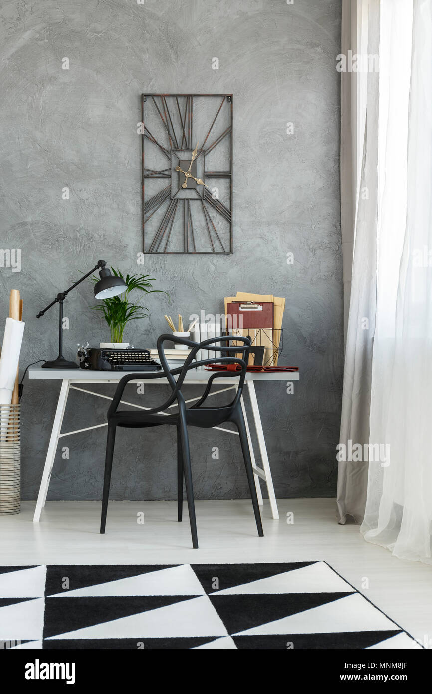 Designer clock on textured wall above desk with lamp in dark workspace ...