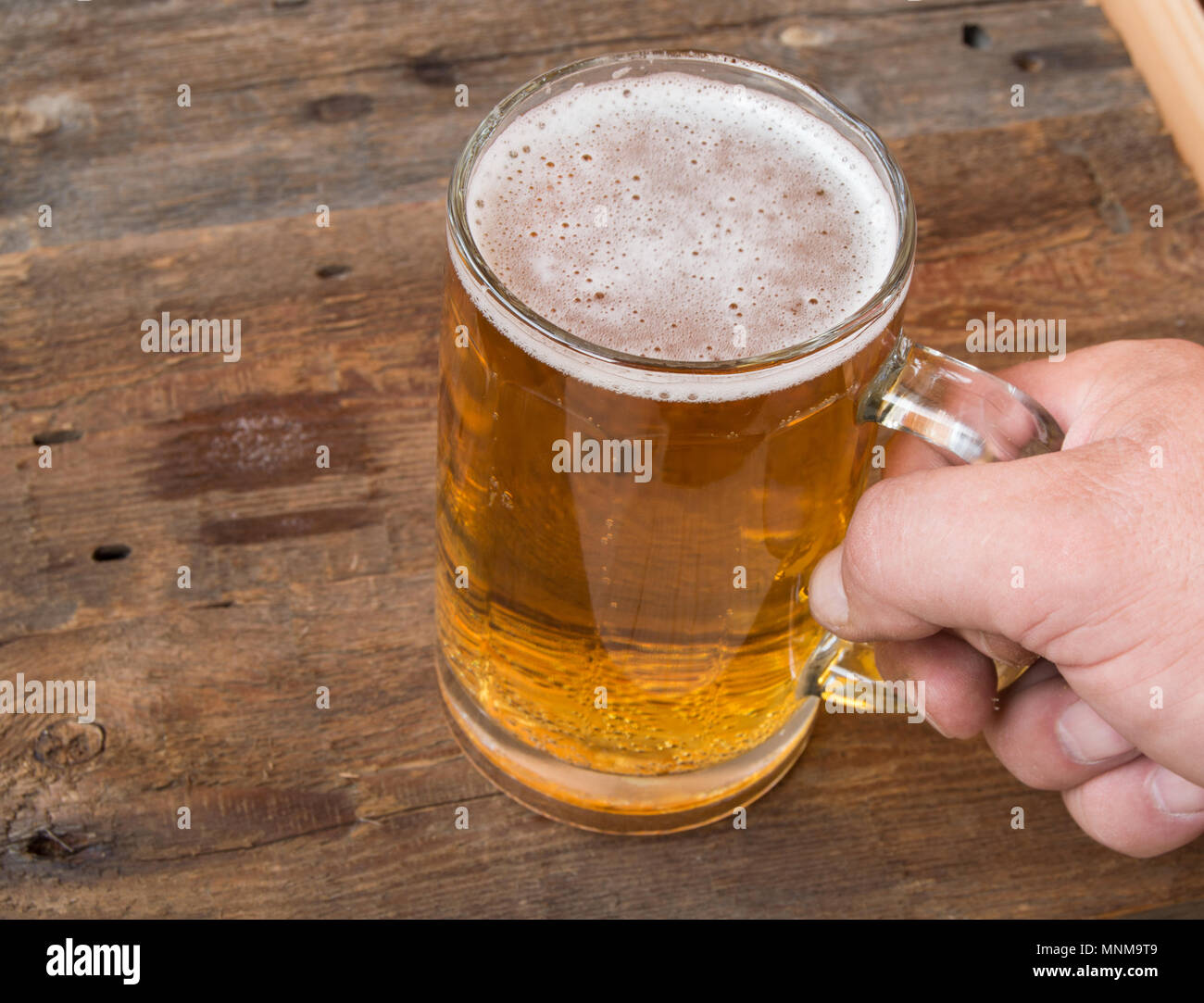 Men's hand holds a mug of light beer on dark vintage wooden boards ...