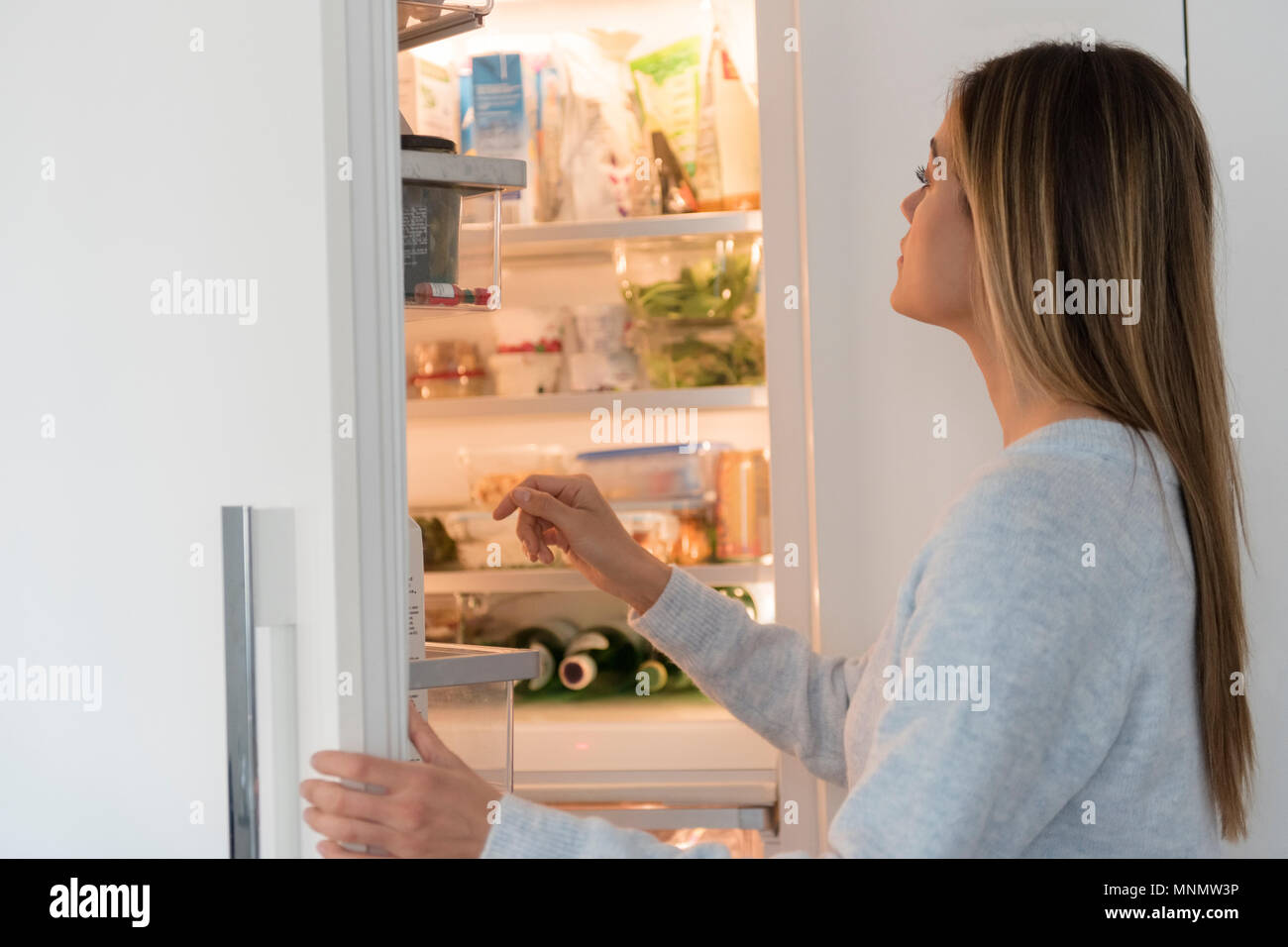 Young woman looking into refrigerator Stock Photo - Alamy