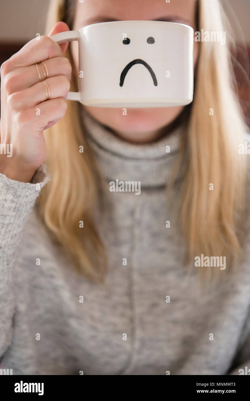 Woman holding mug with sad face in front of face Stock Photo - Alamy