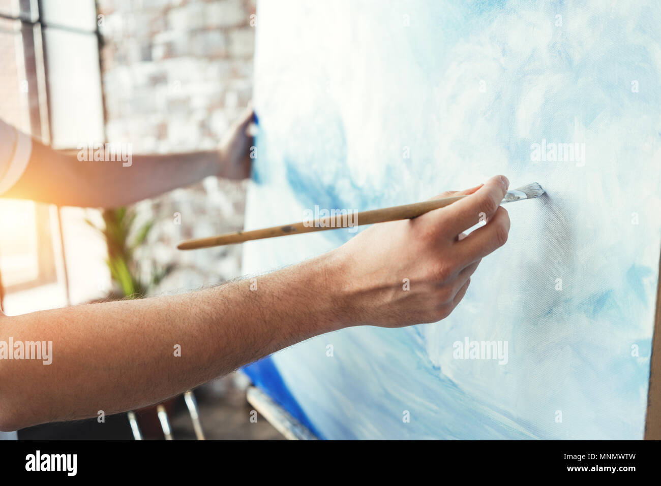 Male hand of artist closeup holding paintbrush on background of canvas ...