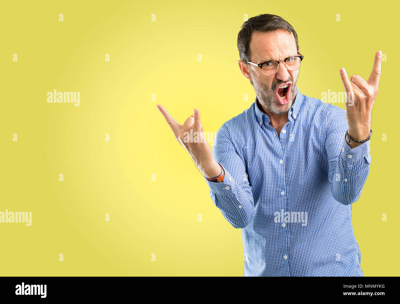 Handsome middle age man making rock symbol with hands, shouting and ...