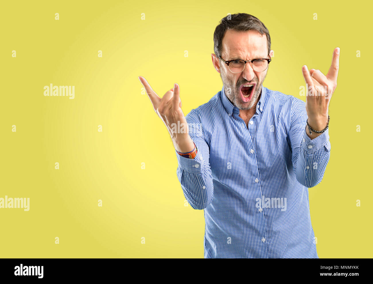 Handsome middle age man making rock symbol with hands, shouting and ...