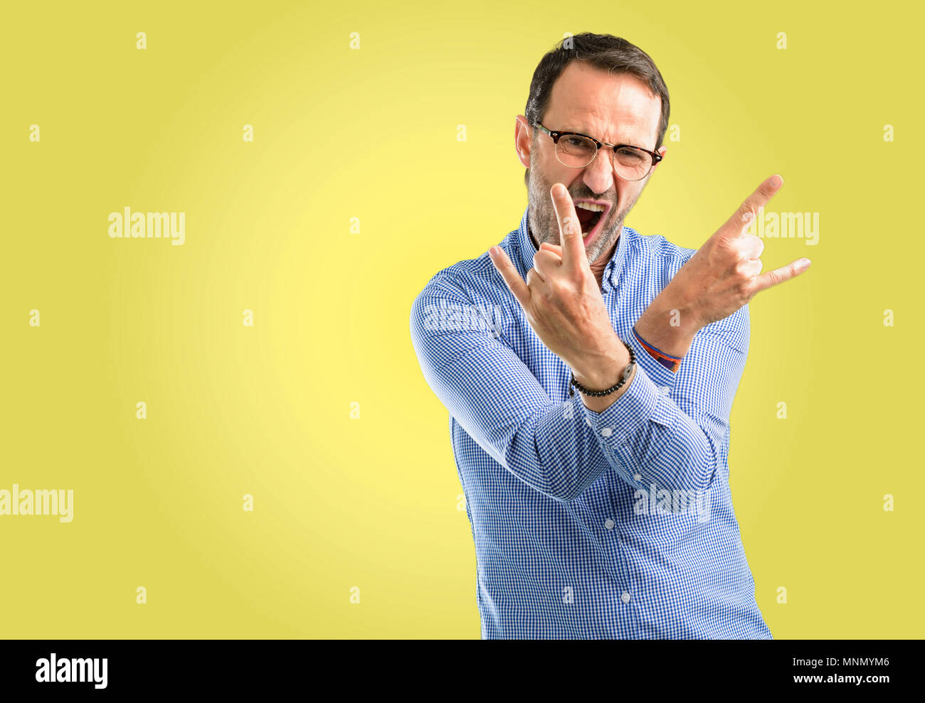 Handsome middle age man making rock symbol with hands, shouting and ...