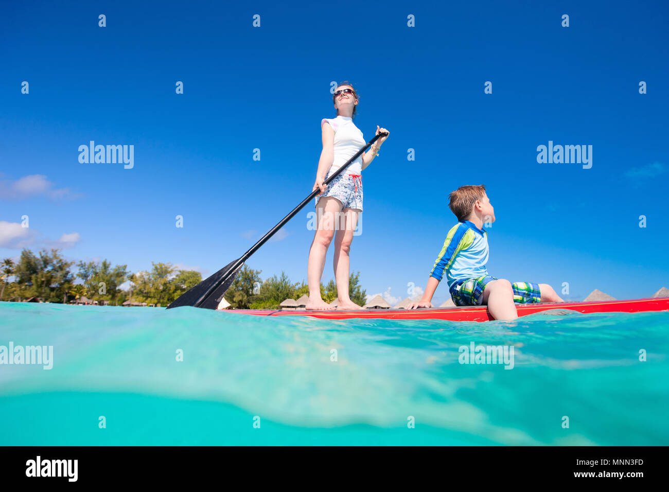 Mother and son paddling on stand up paddle board at tropical ocean ...