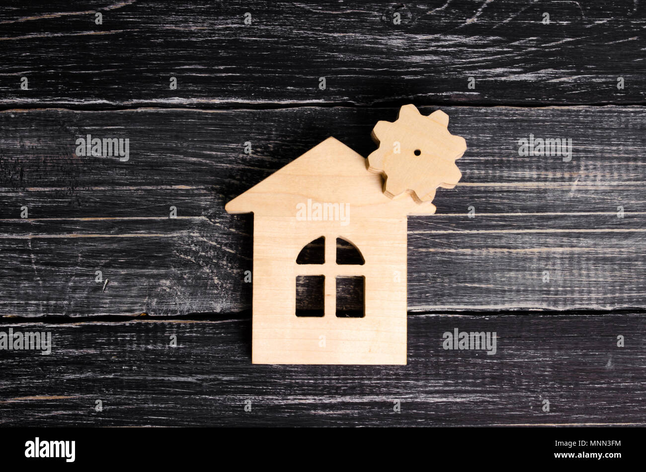 Wooden house with a gear on a background of dark wood. The concept of ...