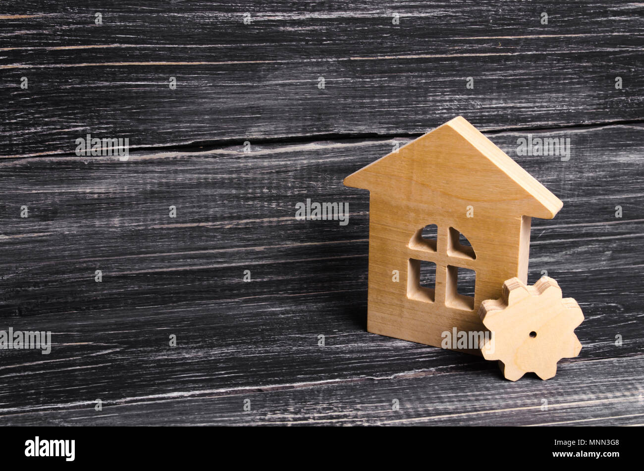 Wooden house with a gear on a background of dark wood. The concept of ...