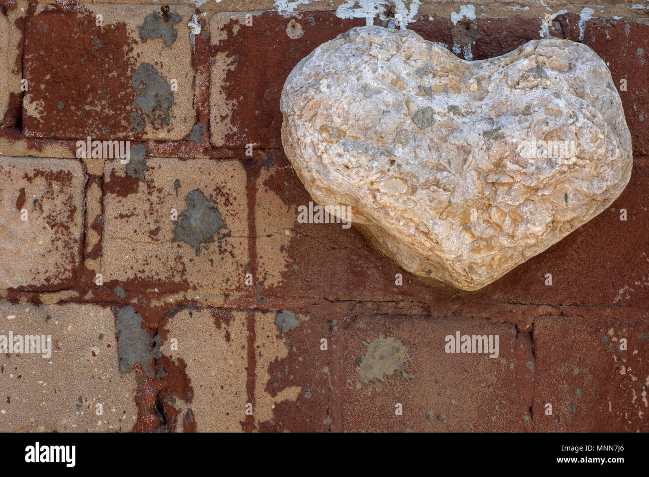 White stone heart, carved from a huge stone, on a brick wall with ...