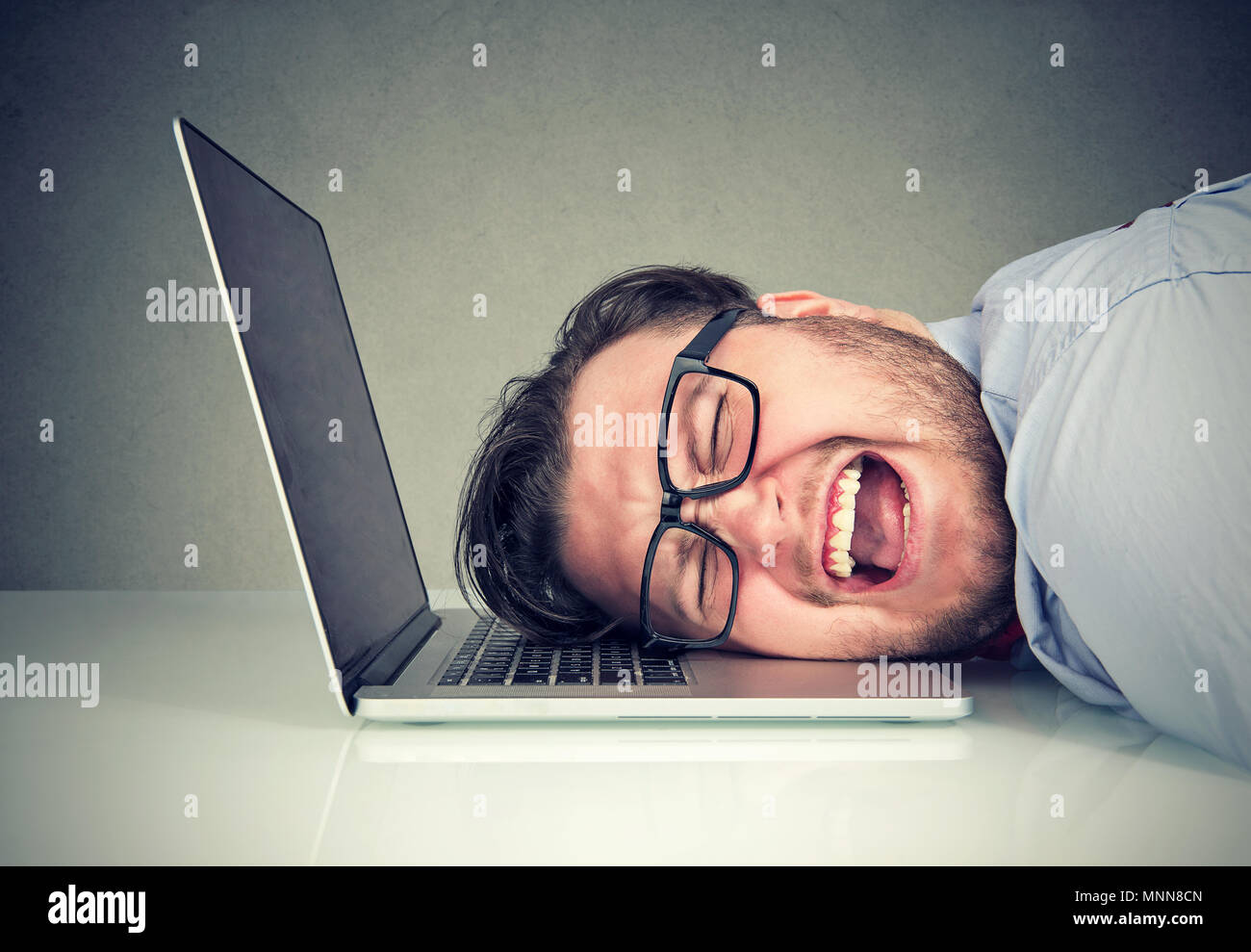 Stressed employee young man sitting at desk with head on laptop feeling ...