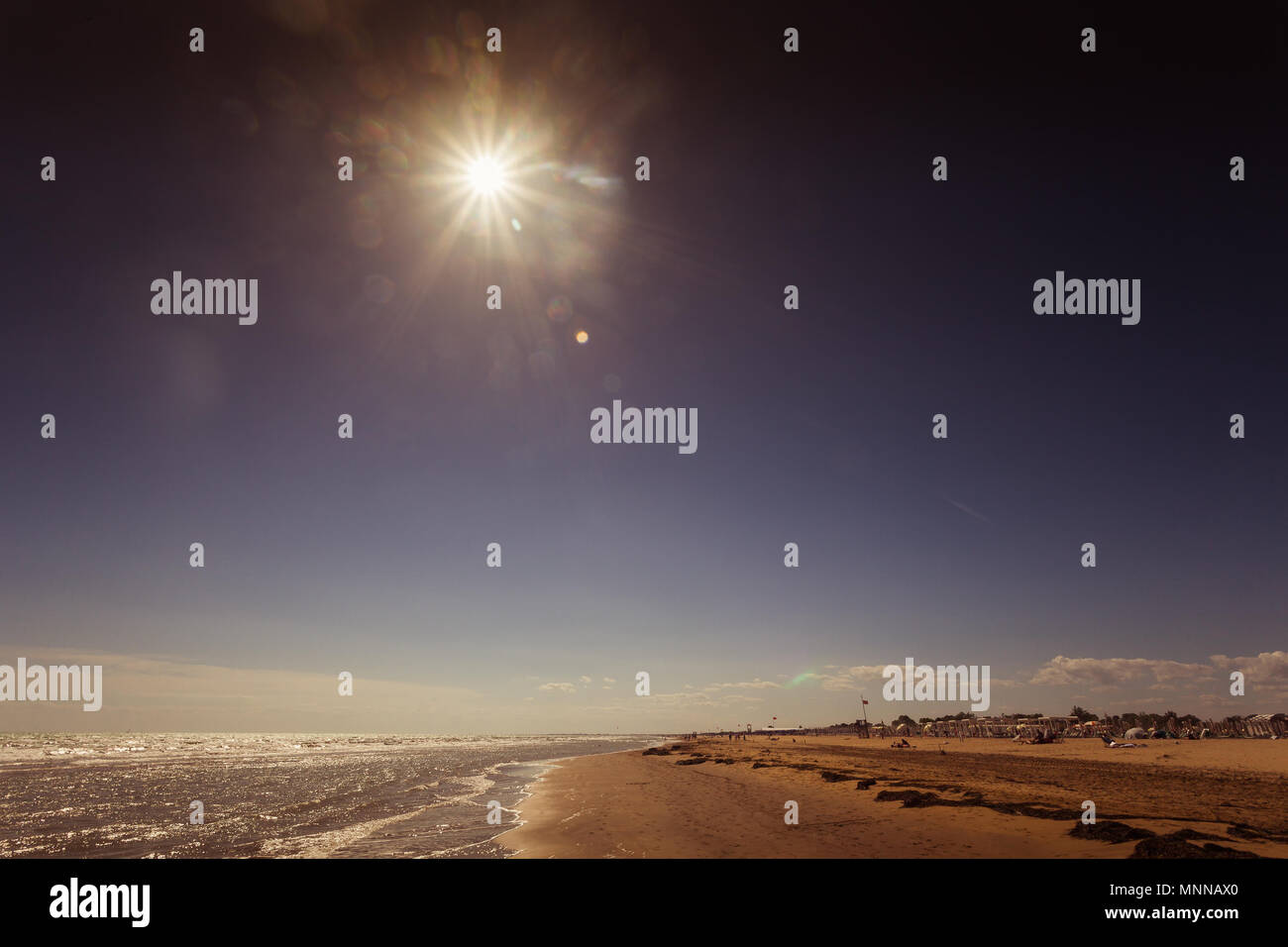 Sun over sandy beach beaten by waves Stock Photo - Alamy