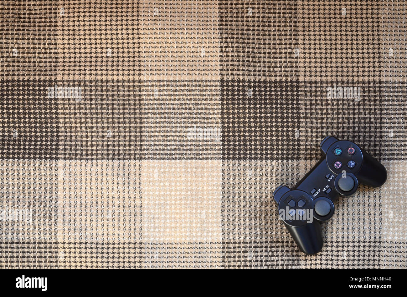 Modern black video game controller lies on a checkered beige and black ...