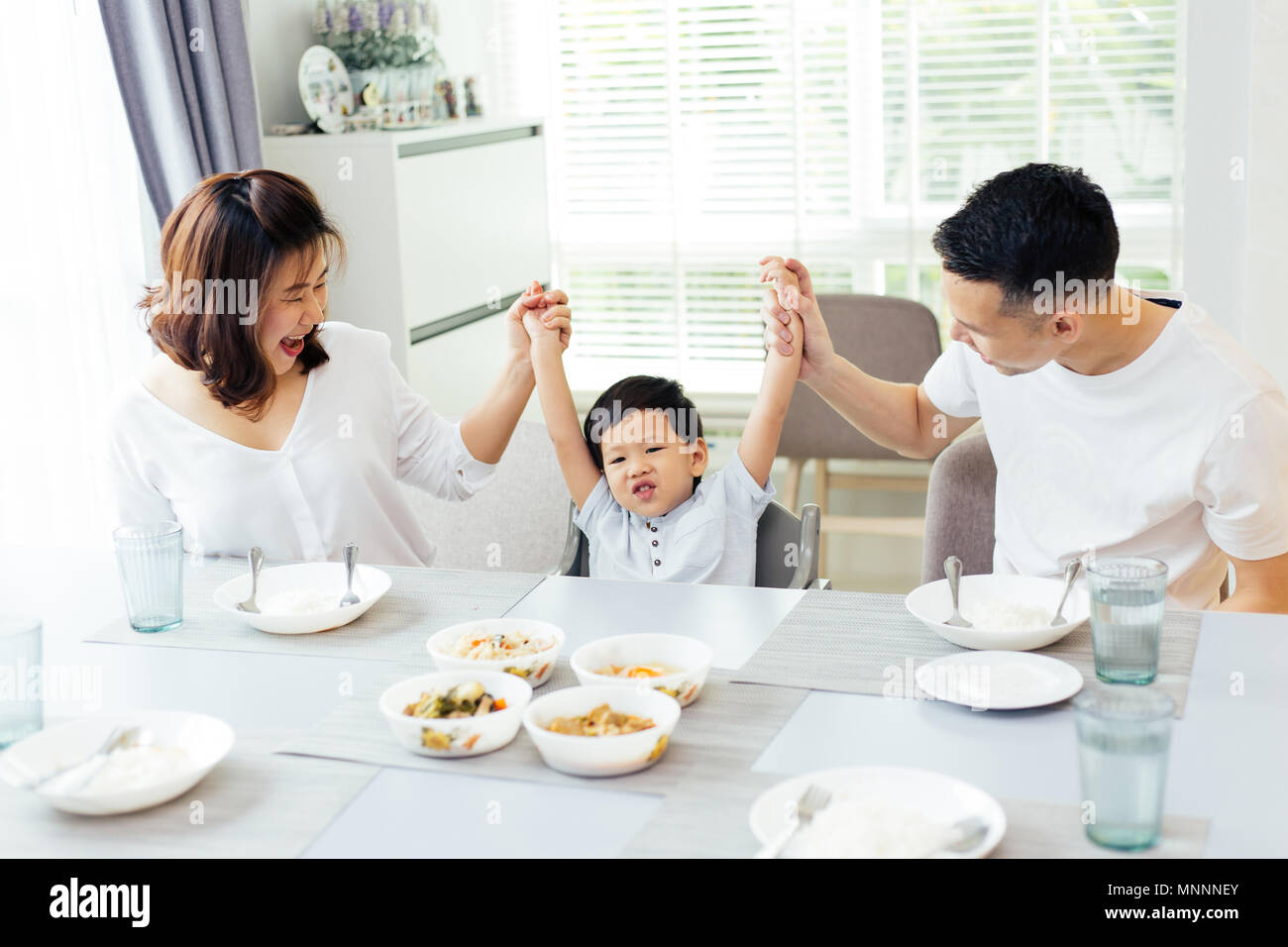 Happy Asian family raising child's hands up and smiling while having a ...