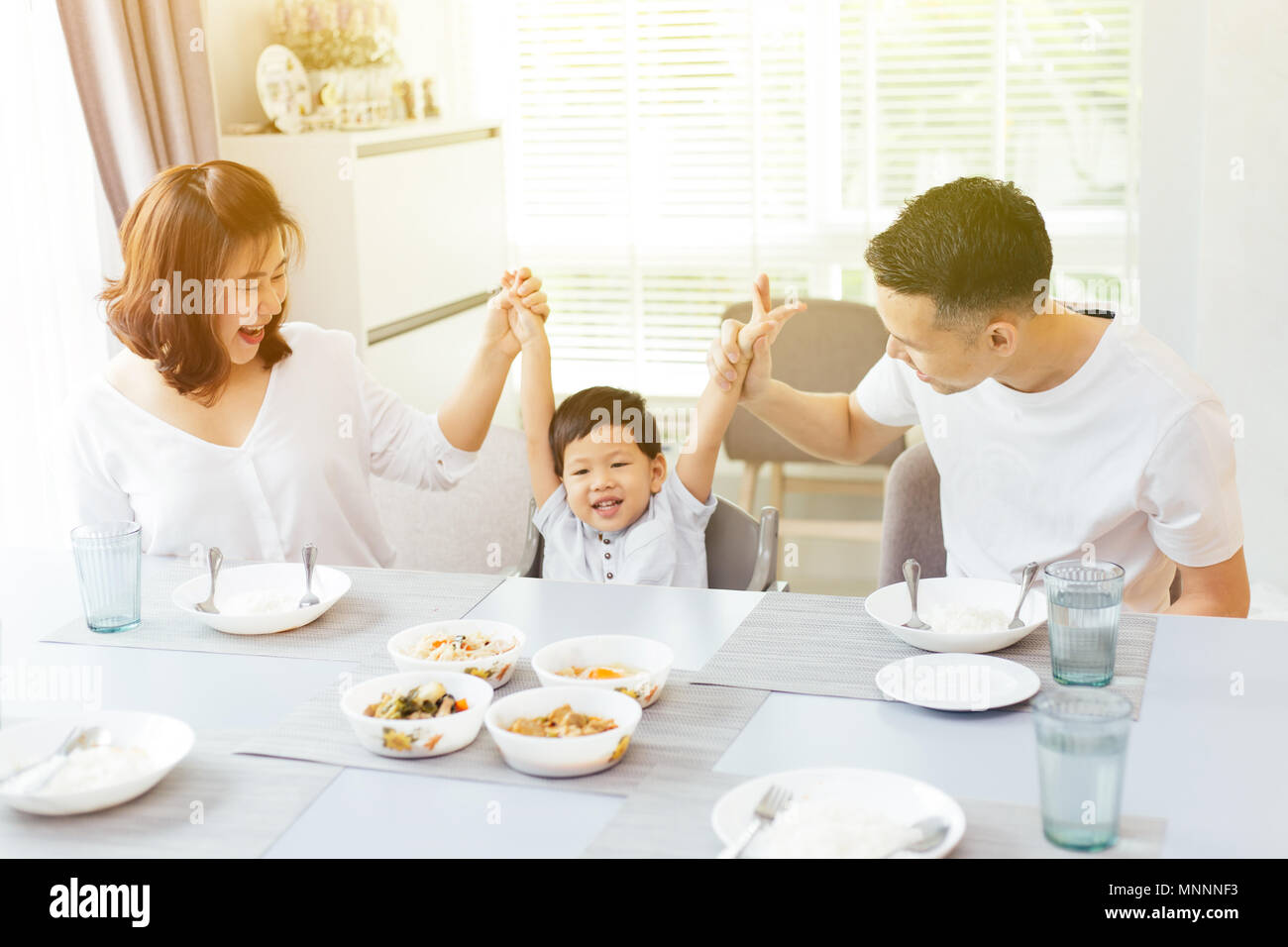 Happy Asian family raising child's hands up and smiling while having a ...