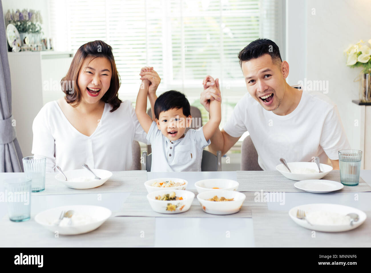 Happy Asian family raising child's hands up and smiling while having a ...