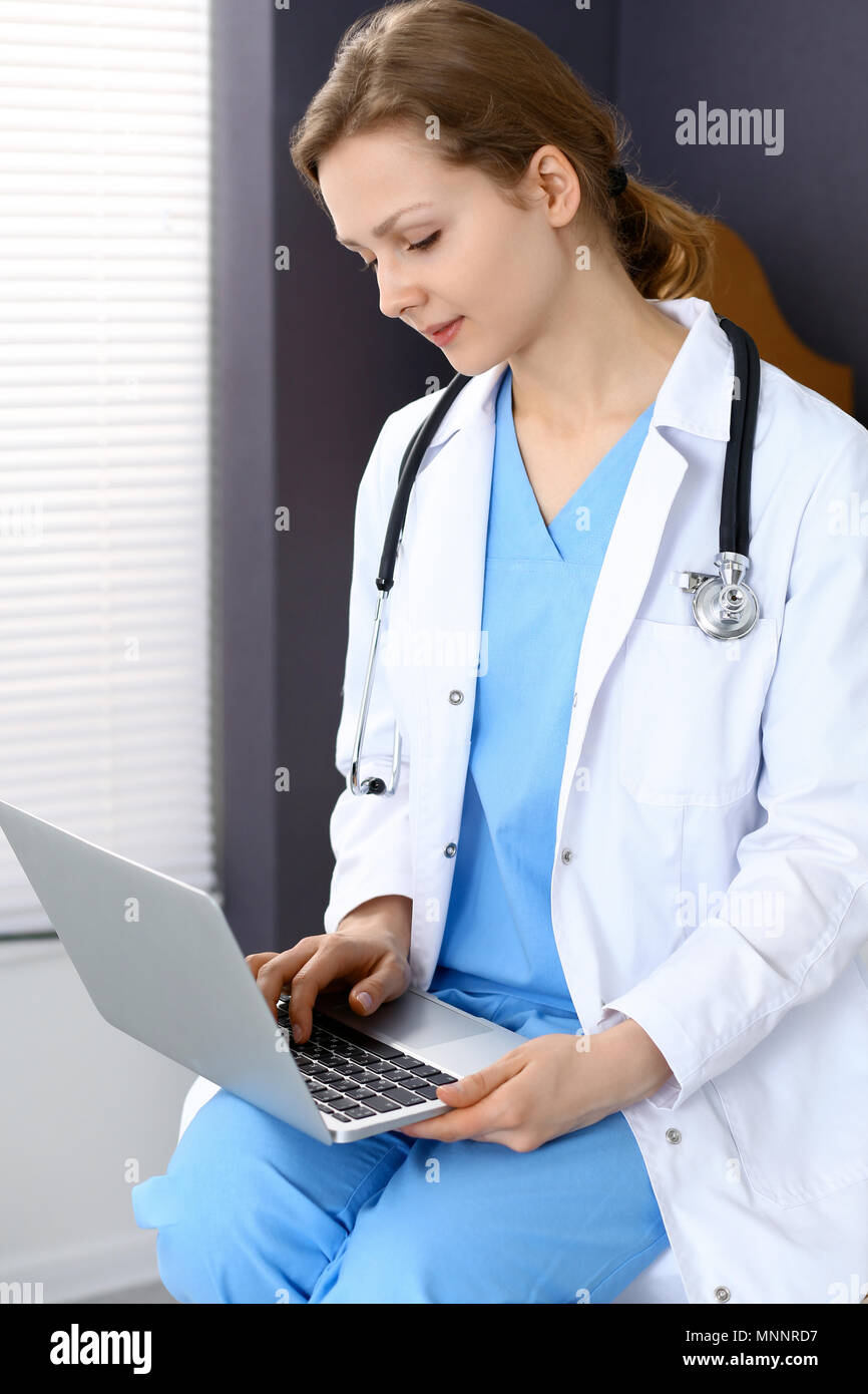 Woman doctor typing on laptop computer while working in hospital office ...