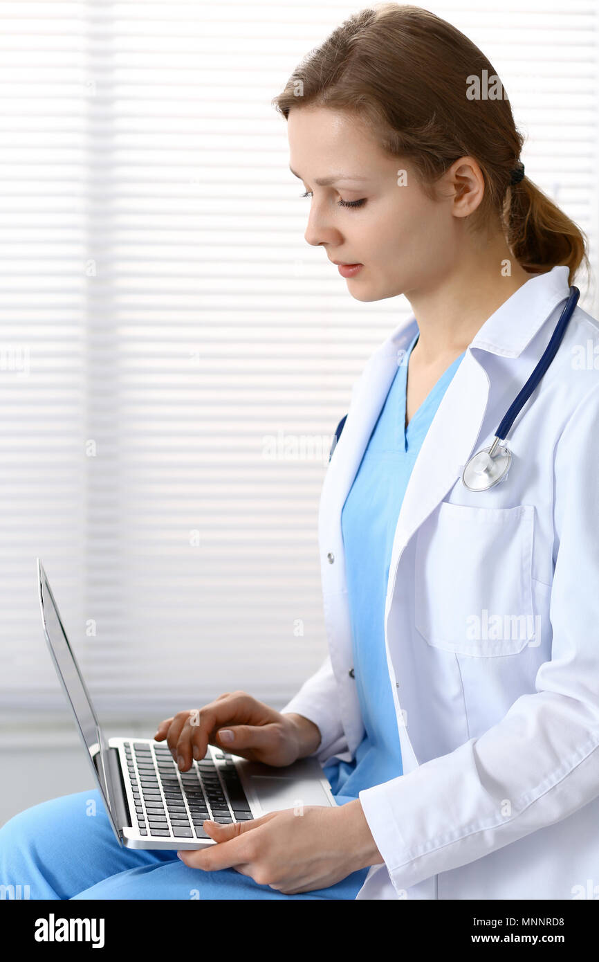 Woman doctor typing on laptop computer while working in hospital office ...