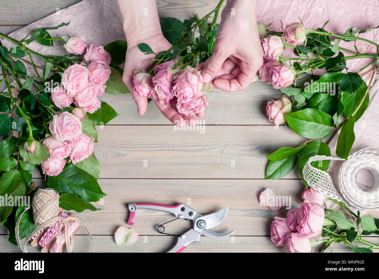 Florist at work. Elegant female hands collect a wedding bouquet of pink roses. People in the ...