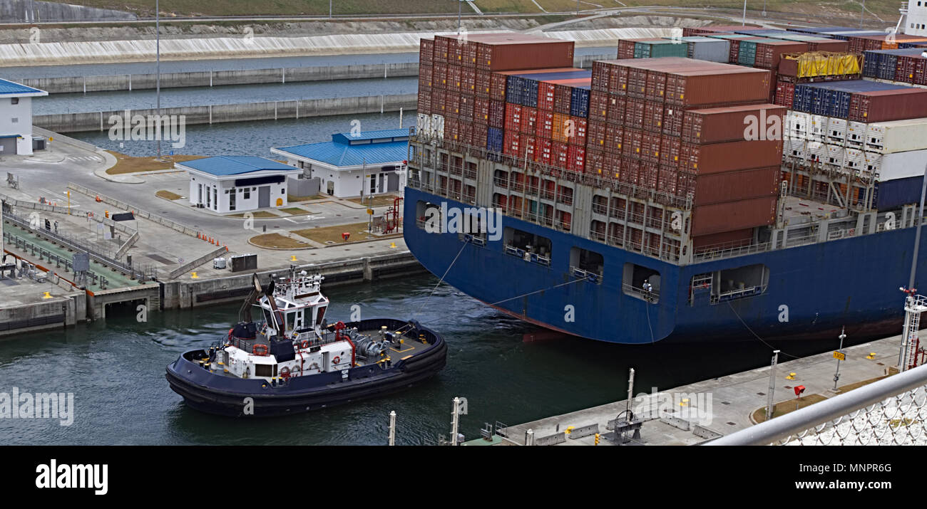 a tug boat works with a huge container ship in a canal to pull or push ...