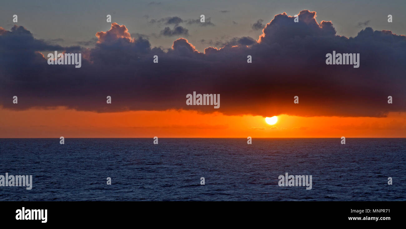 a glorious orange and red sun sets among the clouds in the caribbean ...