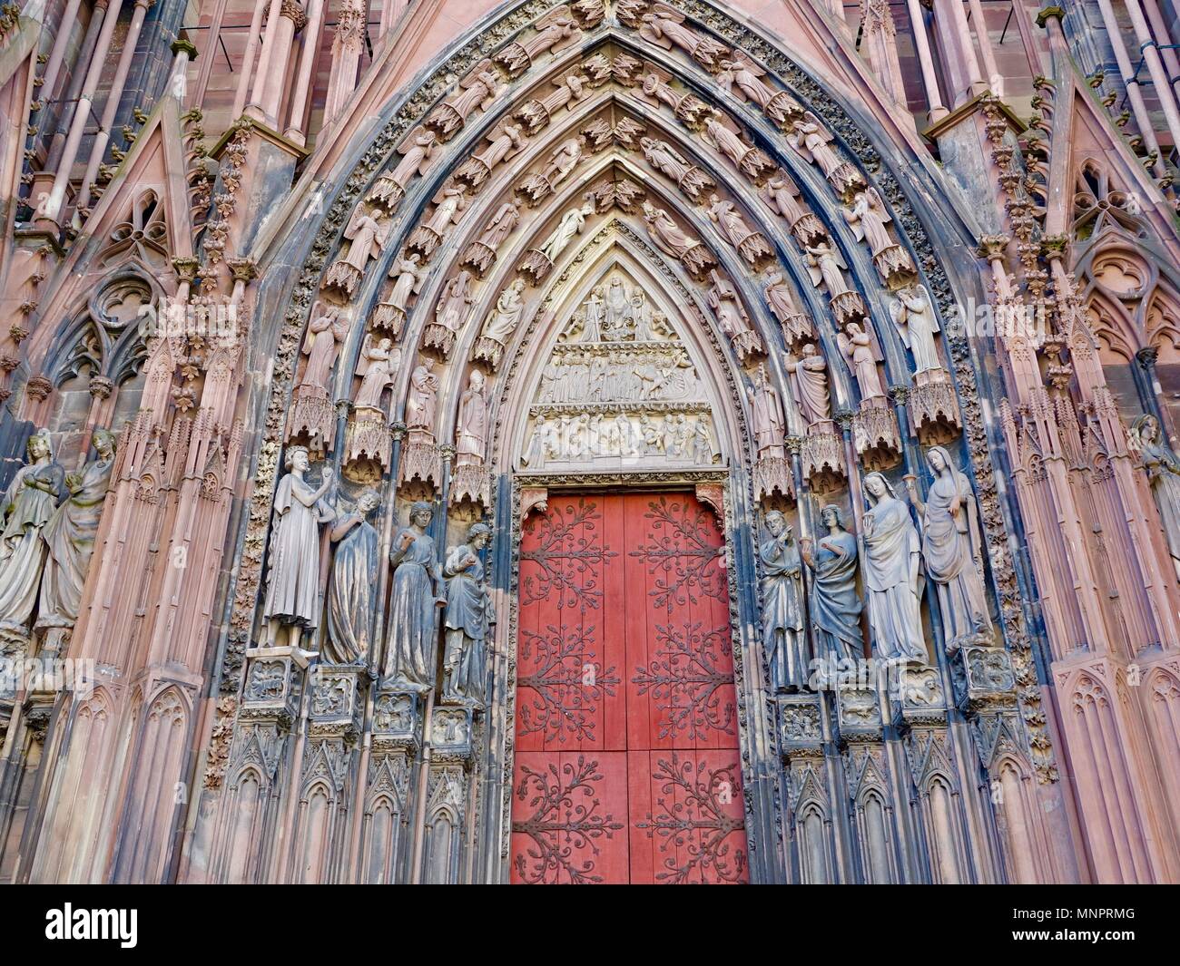 An arched entryway surrounded by carvings of saints frame the red doors ...