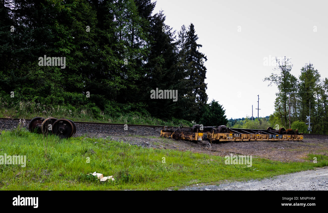 An overturned derailed railroad car lying next to the tracks in pieces ...