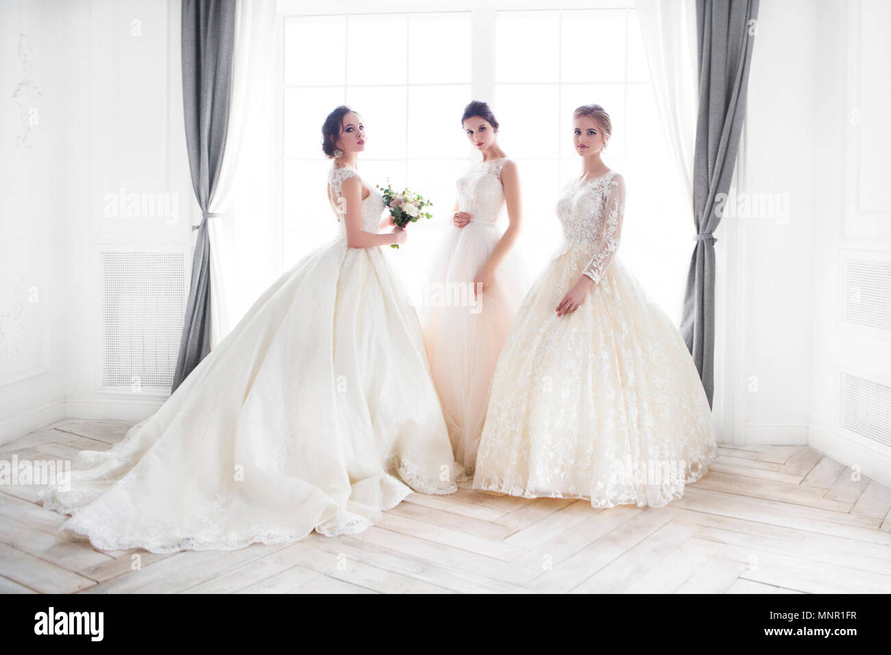 Three young woman with bouquets wearing wedding dresses Stock Photo - Alamy
