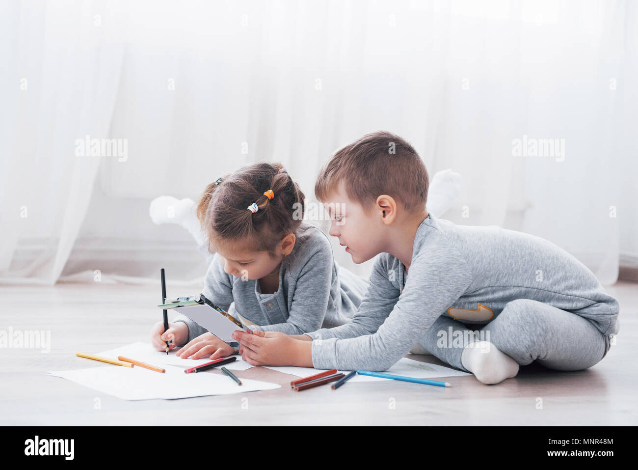 Children lie on the floor in pajamas and draw with pencils. Cute child ...