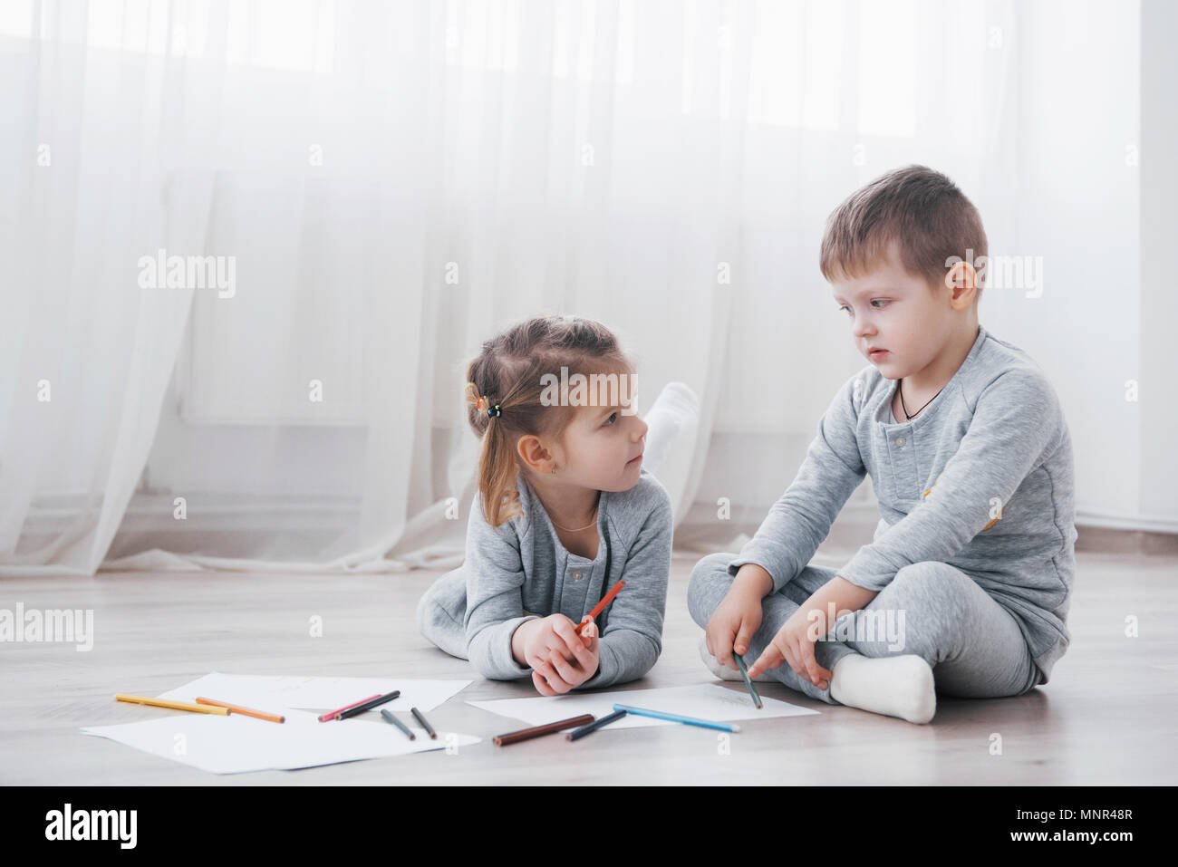 Children lie on the floor in pajamas and draw with pencils. Cute child ...