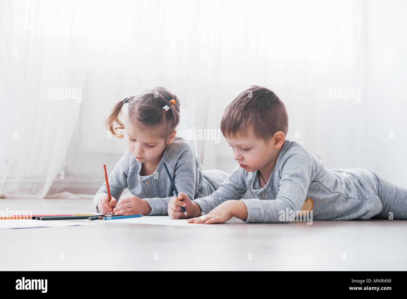 Children lie on the floor in pajamas and draw with pencils. Cute child ...