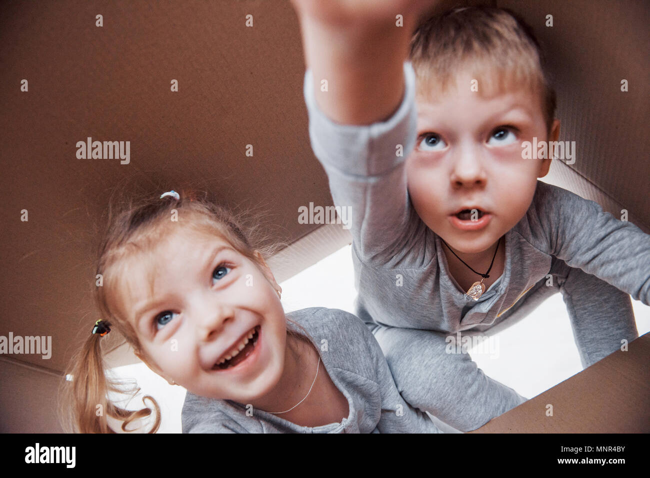 Two a little kids boy and girl opening a cardboard box and climbing in ...