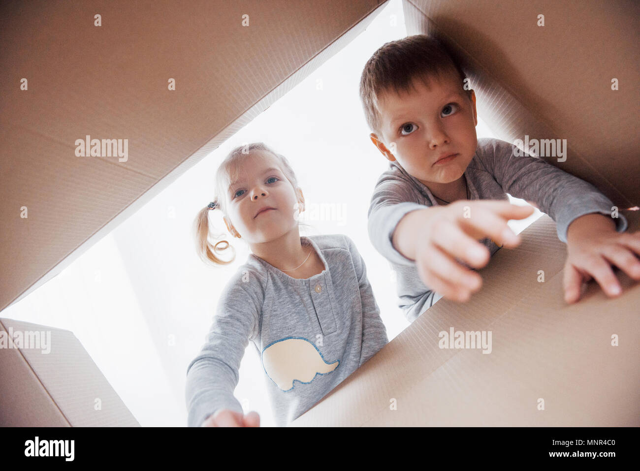 Two a little kids boy and girl opening cardboard box and looking inside ...