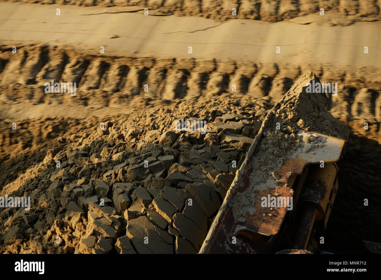 Close-up, detail, crumbling sand falling in front of bulldozer scraper ...
