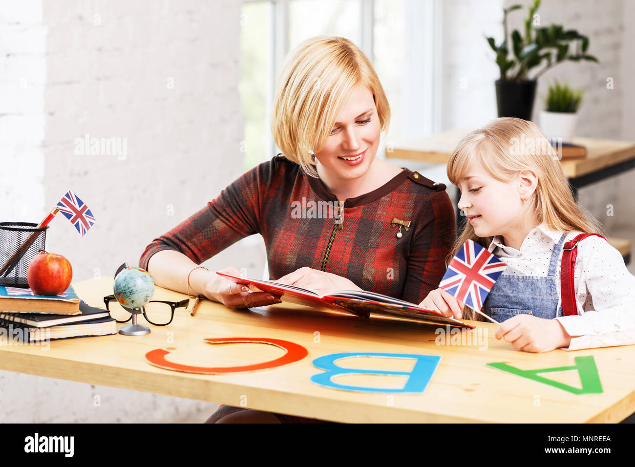Elegant English educator studying with kid girl, reading book on the ...