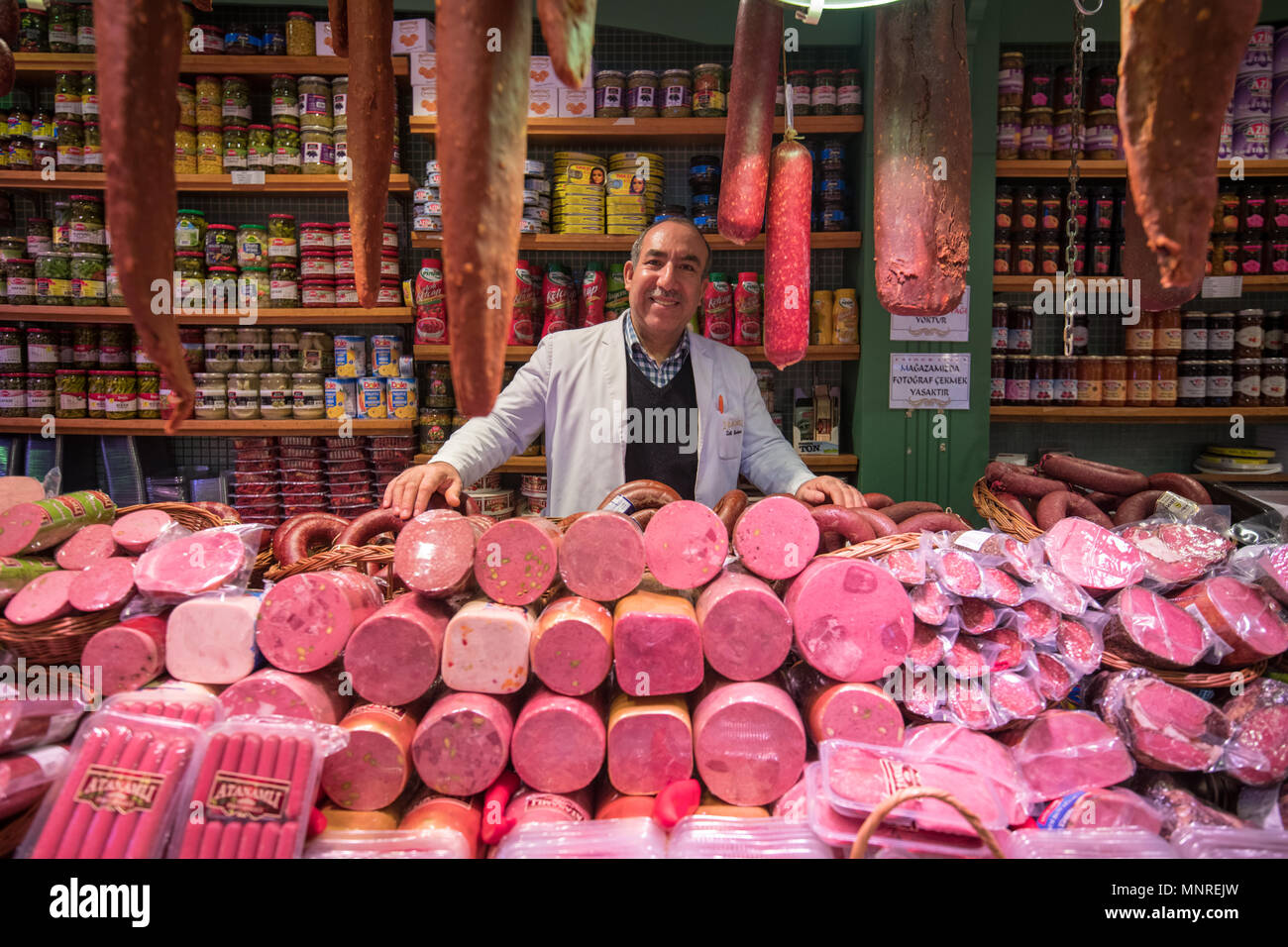 A smiling adult male merchant stands behind counter full of various ...