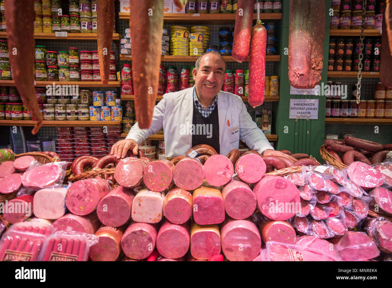 A smiling adult male merchant stands behind counter full of various ...