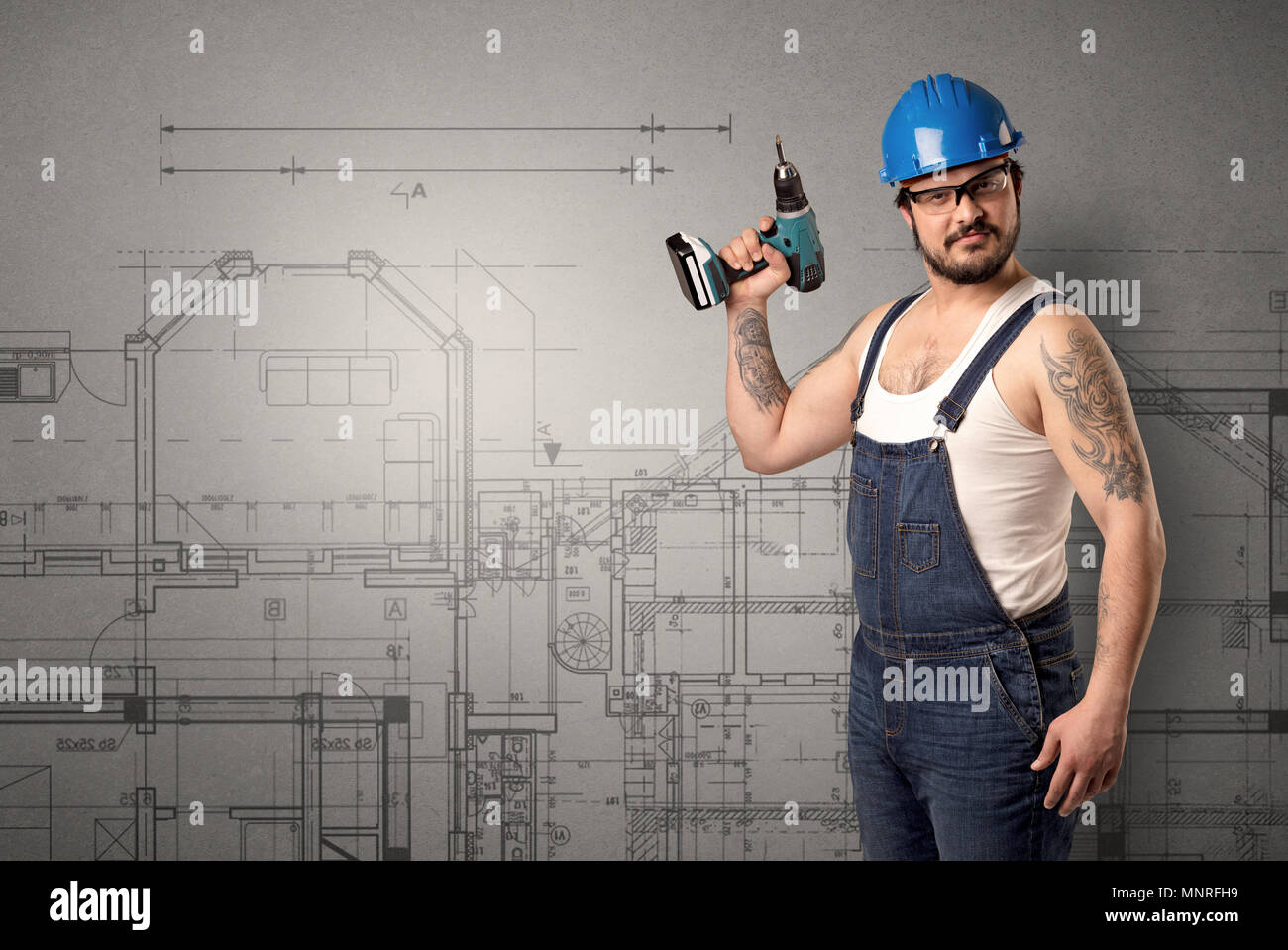 Worker standing with tool in his hand in front of technical drawings ...