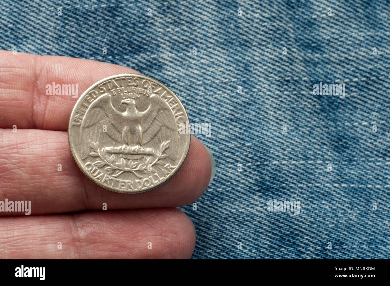 A quarter of a dollar lies on the fingers of the hand, a blue denim ...