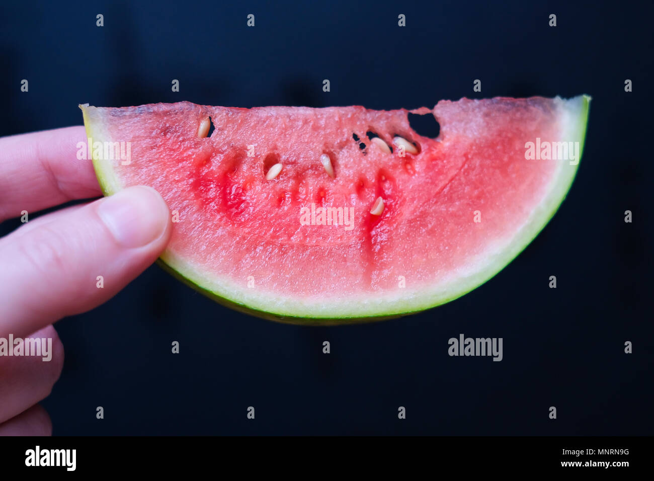 A slice of juicy fresh mini watermelon in a female hand on a dark ...