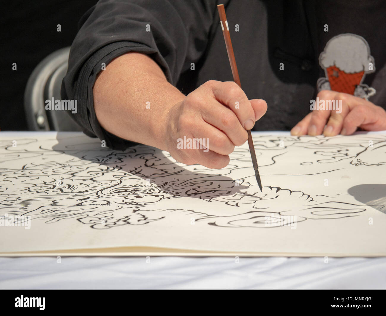 An artist's hand drawing Asian artwork on a canvas using ink pen Stock ...
