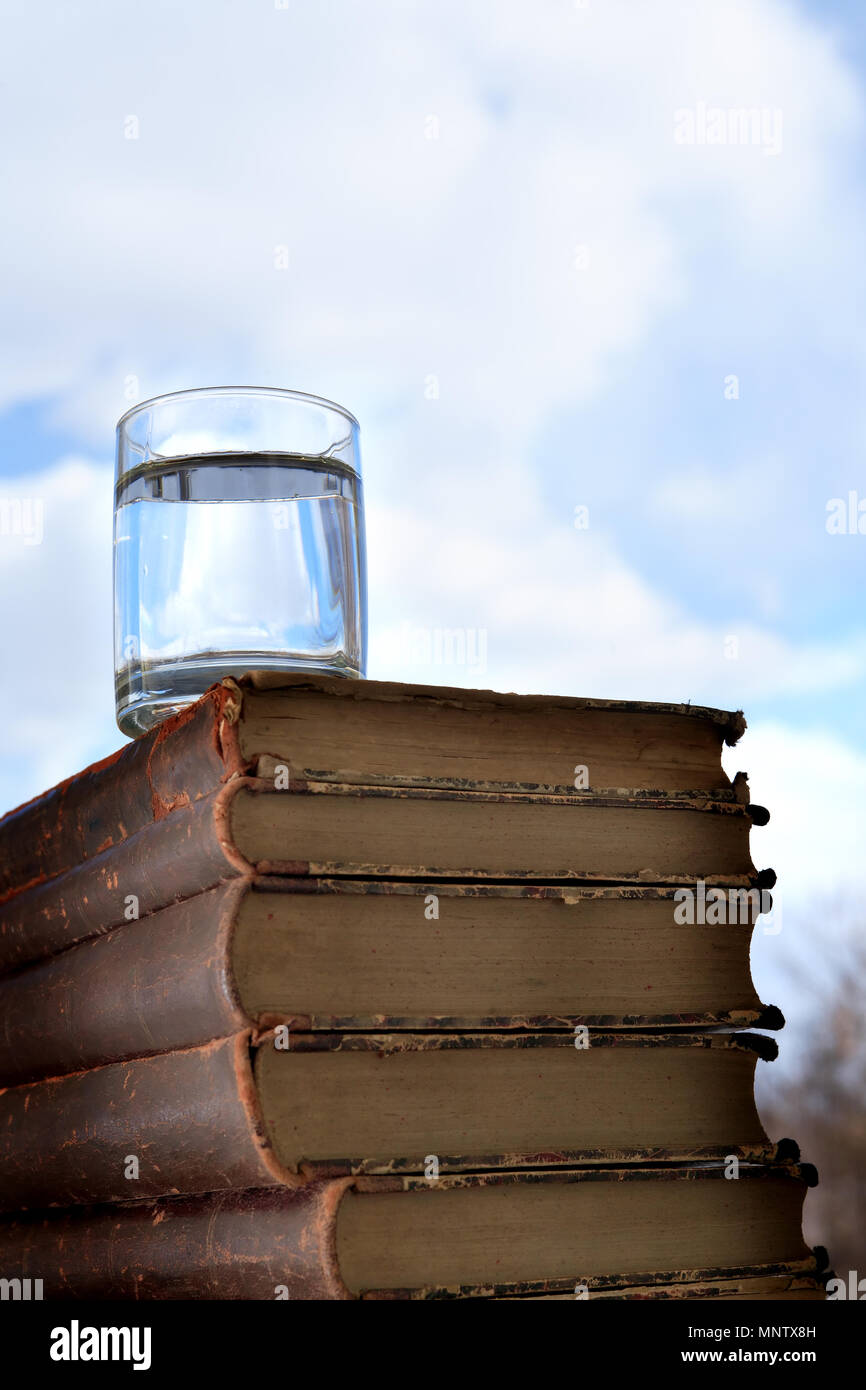 Glass of water on stack of old books on blue sky background with free ...