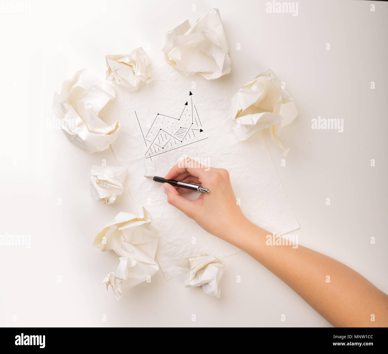 Female hand next to a few crumpled paper balls drawing a progress chart ...