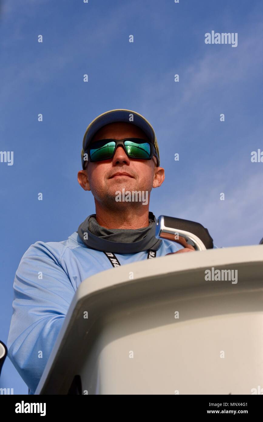 Captain at wheel of fishing boat, wearing reflective sunglasses and cap ...