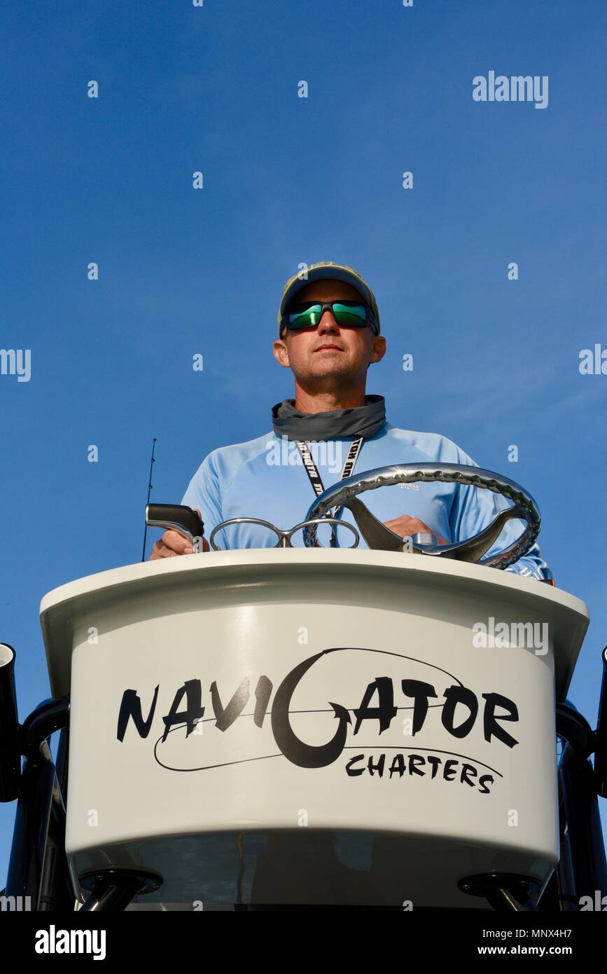 Captain at wheel of fishing boat, wearing reflective sunglasses and cap ...