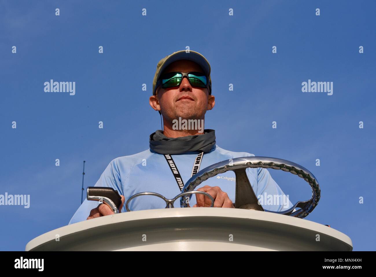 Captain at wheel of fishing boat, wearing reflective sunglasses and cap ...