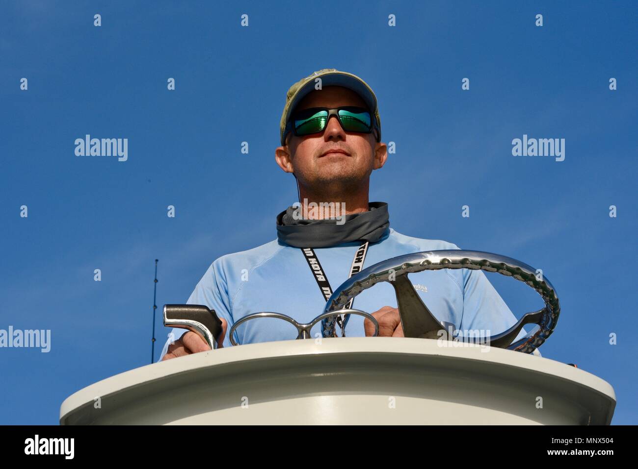Captain at wheel of fishing boat, wearing reflective sunglasses and cap ...