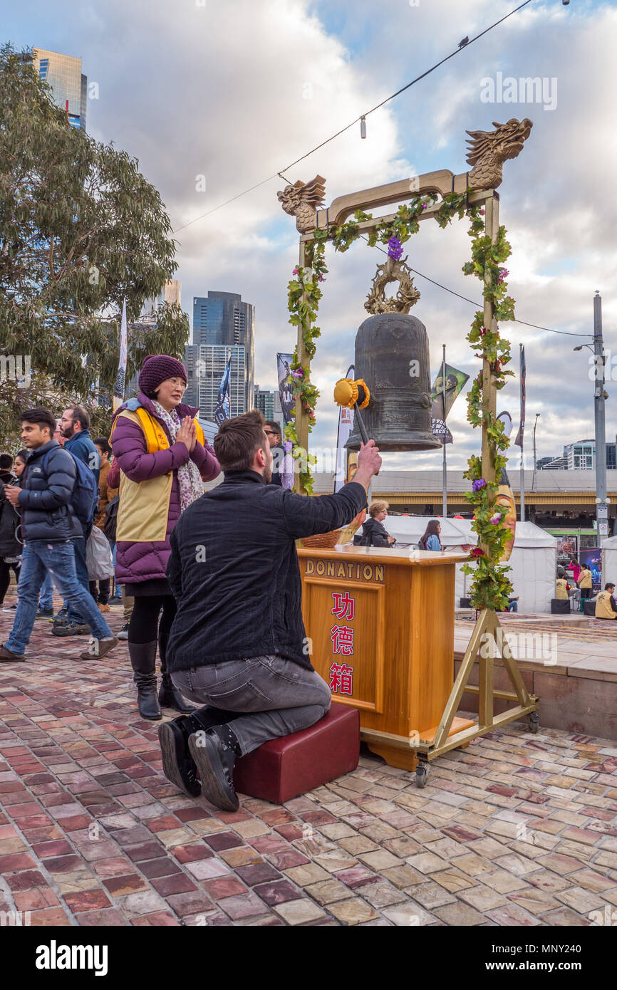 Middle aged man hitting large brass bell with wooden mallet while ...