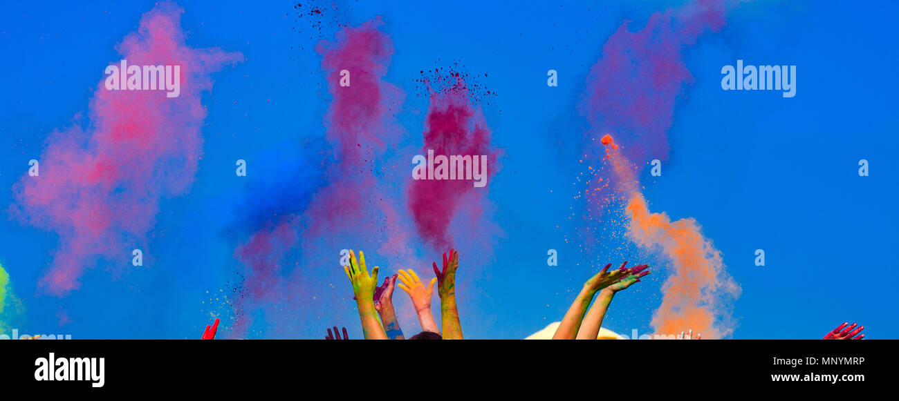 At the color Holi festival, hands in the air, blue sky behind Stock ...