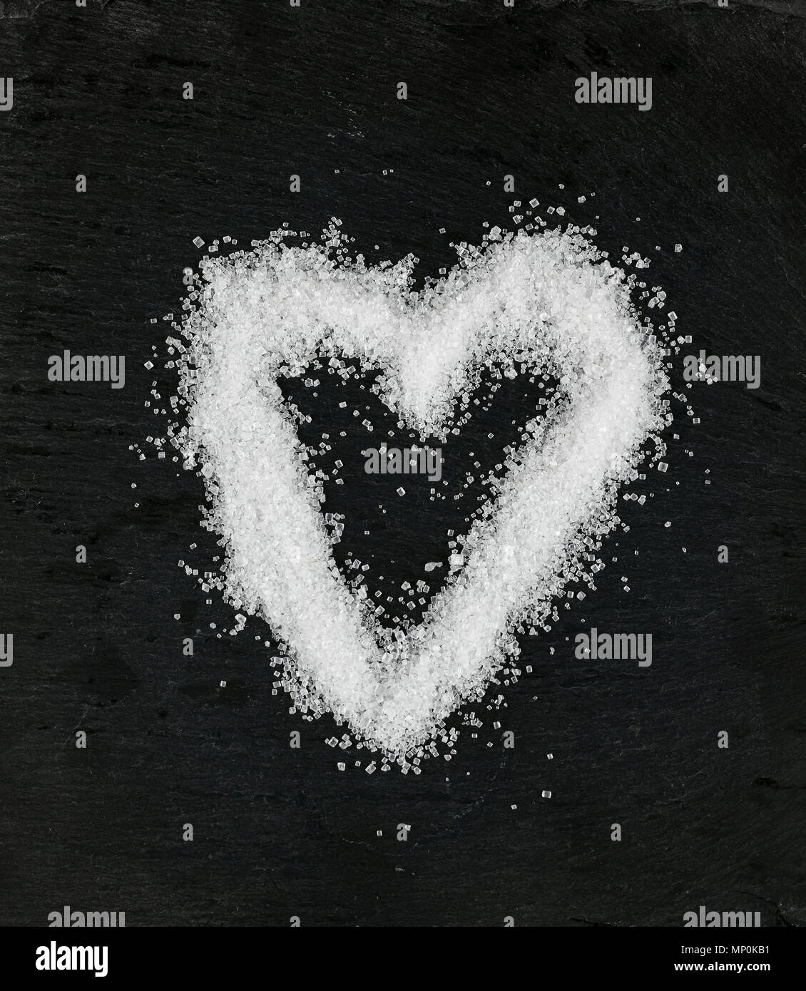 A heart-shaped pile of sugar on black stone, danger and health risks of ...